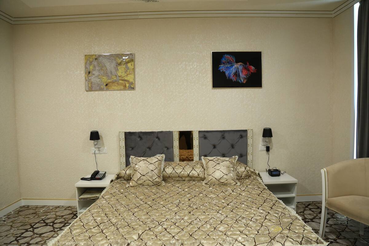 Quarto de hotel com uma cama grande, duas mesas de cabeceira, uma cadeira e obras de arte nas paredes.