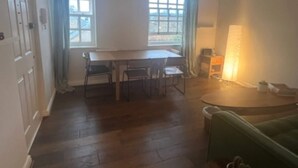 Um quarto espaçoso com uma mesa de jantar e cadeiras, um sofá verde, uma luminária e uma janela com cortinas.