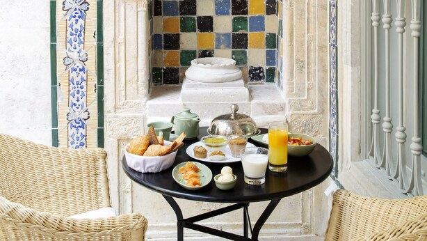 Uma área de refeições com uma mesa posta para o café da manhã, com pão, doces e uma bebida de frutas.