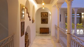 Um corredor com piso de mármore, um banco de madeira e uma escada com corrimão.