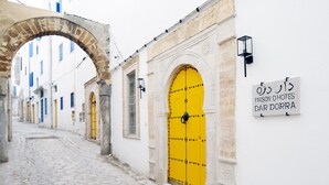 Uma rua de paralelepípedos estreita com uma porta amarela e uma placa em idioma estrangeiro.
