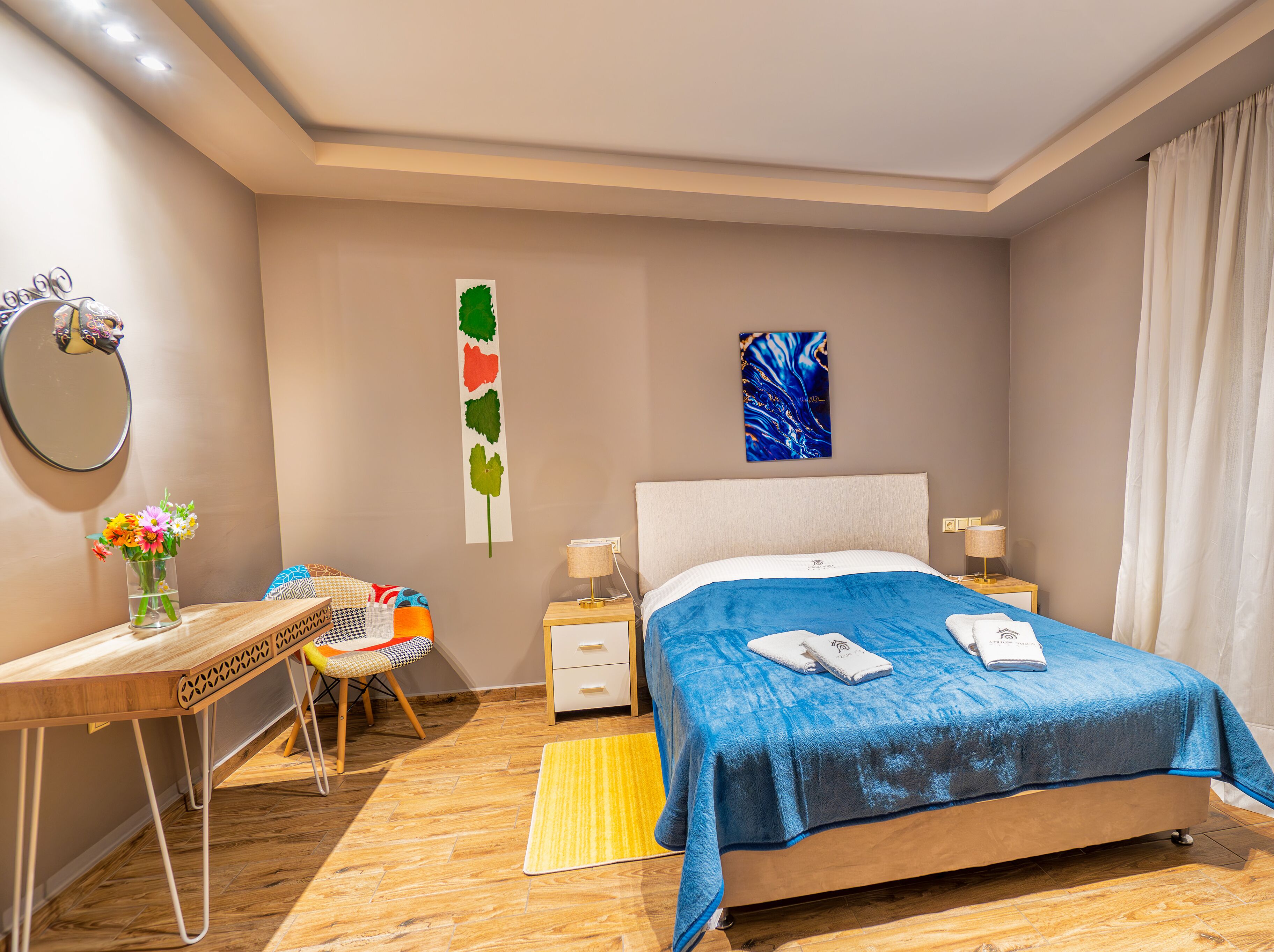 Quarto de hotel com cama, mesas de cabeceira, escrivaninha, cadeira, espelho e um ornato na parede.