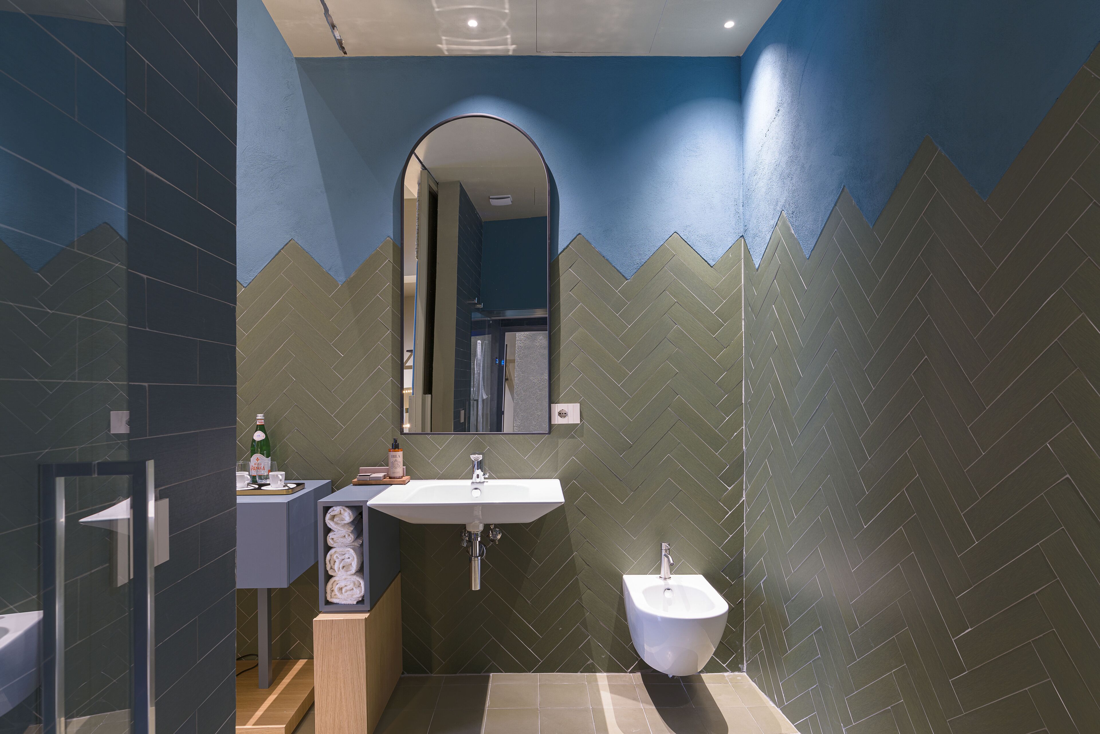 Uma casa de banho moderna com parede em padrão herringbone, uma pia, um bidé e cabine de duche em vidro.