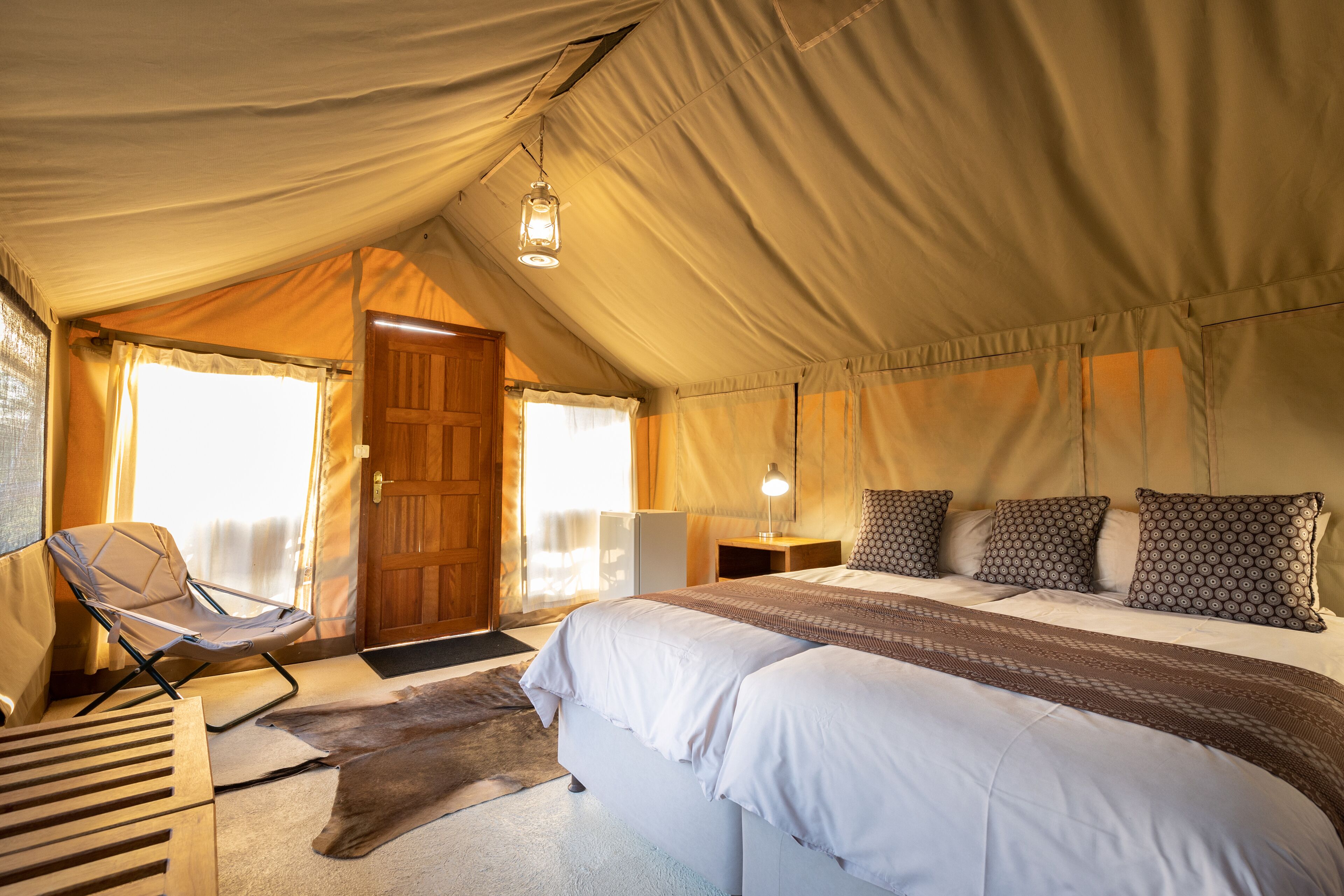 Um quarto com tenda, uma cama, uma cadeira, um abajur e uma porta.