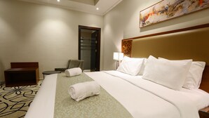 Quarto de hotel com uma cama grande, uma cadeira, uma mesa pequena e um quadro na parede.