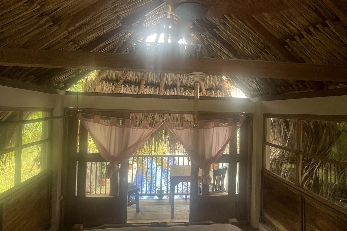 Quarto com telhado de palha, uma cama e vista para o exterior.