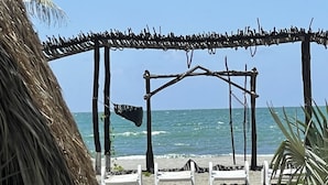 Uma praia com uma estrutura de palha e espreguiçadeiras brancas.