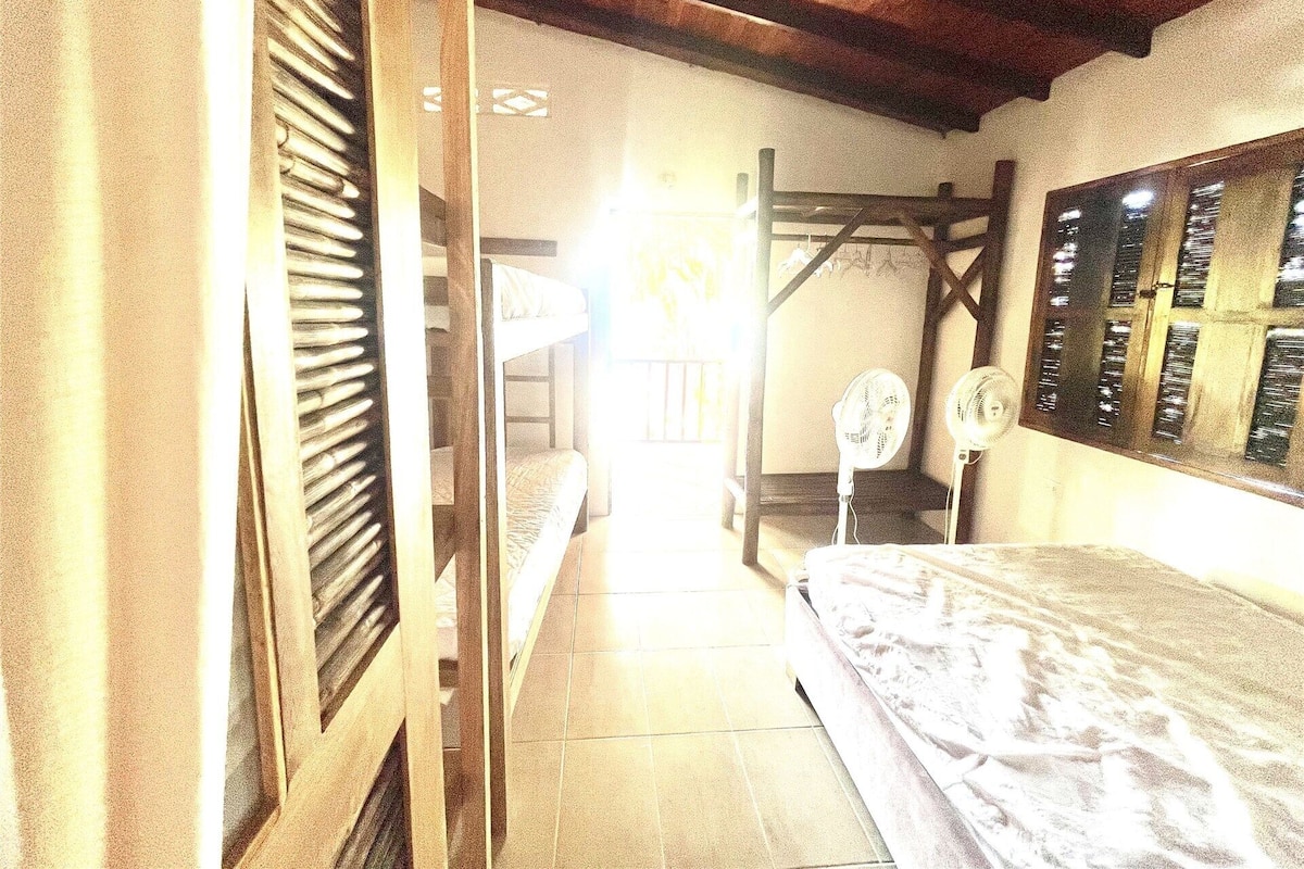 Quarto com beliche, um ventilador e janela com persianas.