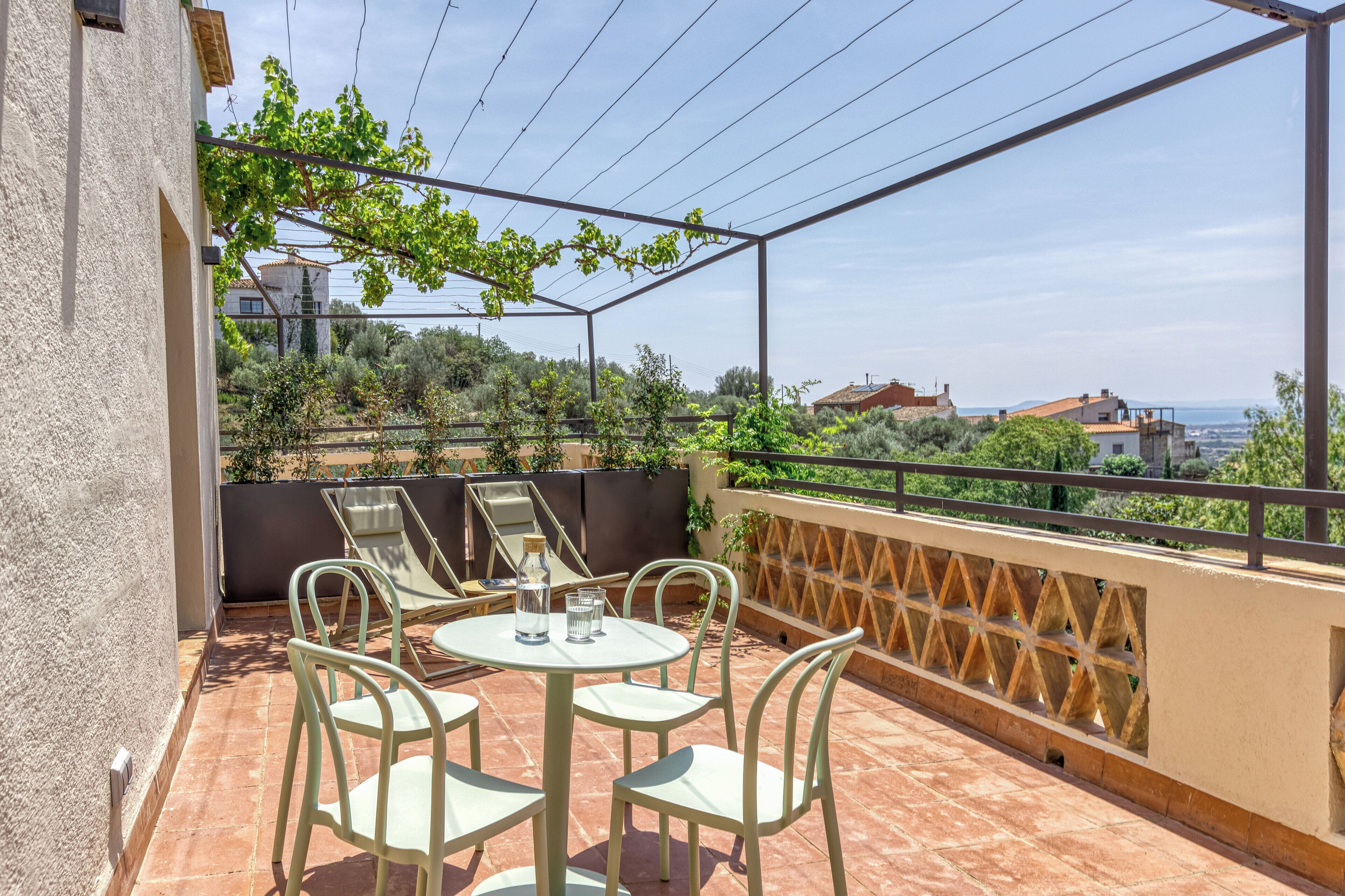 Um terraço com mesa e cadeiras, vista para o campo e um edifício ao fundo.