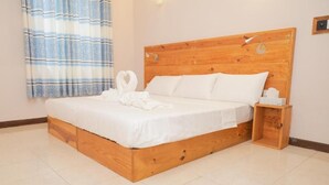 Cama bem arrumada com lençóis brancos e duas toalhas em formato de coração, cabeceira de madeira e uma pequena mesa de cabeceira com uma caixa de lenços.