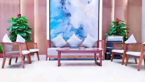 Um hall moderno com um conjunto de sofás, cadeiras e uma mesa de centro. Há duas plantas em vasos e uma grande pintura abstrata na parede.