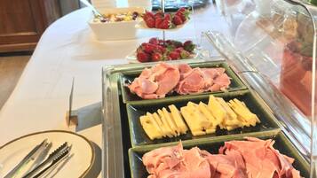 Uma mesa de buffet com diversos alimentos, incluindo presunto, queijo e morangos.