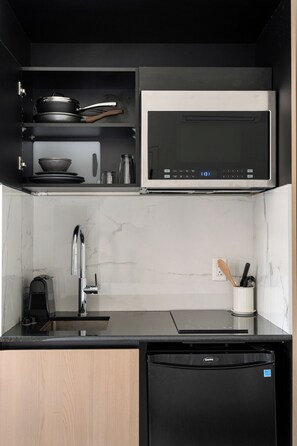 Cozinha compacta com micro-ondas, pia e geladeira preta.