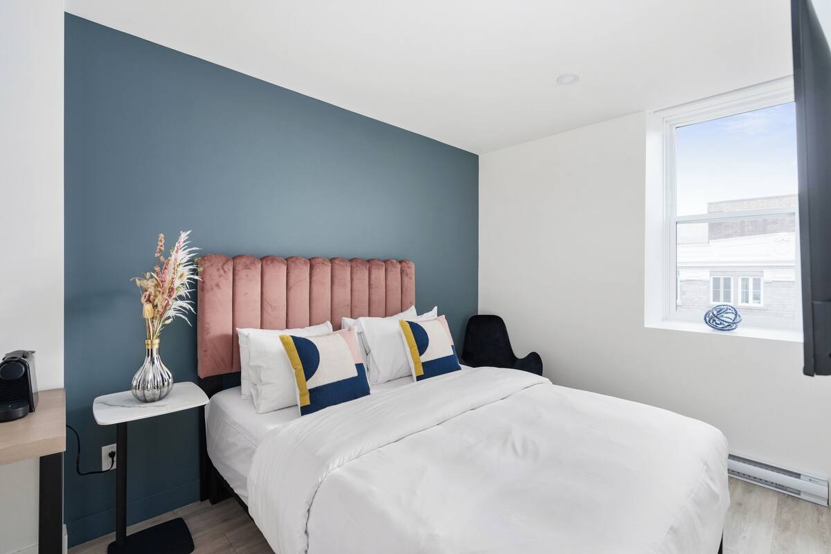 Quarto de hotel moderno com uma cama, uma escrivaninha, um vaso com flores e uma janela com vista.