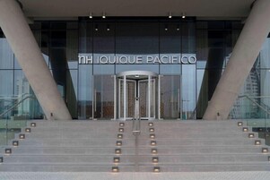 Entrada do NH IQUIQUE PACIFICO, com fachada de vidro e porta giratória.