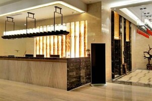 Uma área de recepção com balcão de mármore, luminárias pendentes modernas e um grande painel luminoso vertical.