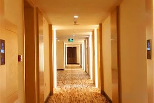 Corredor de hotel com piso coberto por carpete, portas em ambos os lados e uma luz no final.