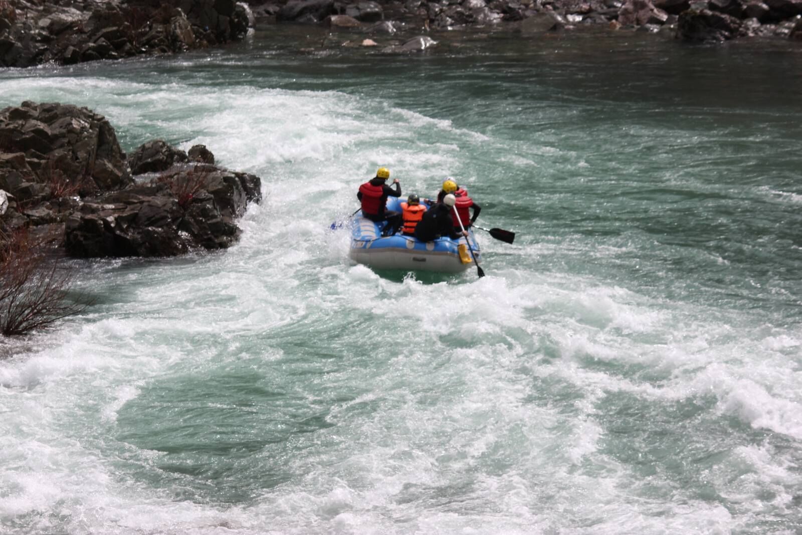 Um grupo de pessoas em uma jangada azul navegando um rio com corredeiras.