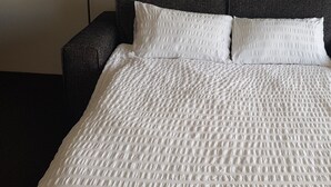Cama bem arrumada com colcha branca texturizada e dois travesseiros.