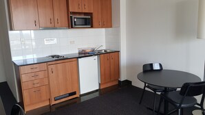Cozinha compacta com armários de madeira, micro-ondas, lava-louças e uma pequena mesa de jantar com cadeiras.