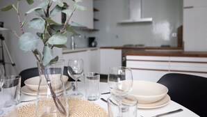 Mesa de jantar posta com copos de vidro transparente, pratos e uma planta decorativa.