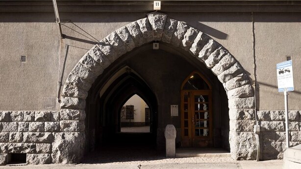 Arcada de pedra que dá acesso à entrada de um edifício, com porta de madeira e uma placa.
