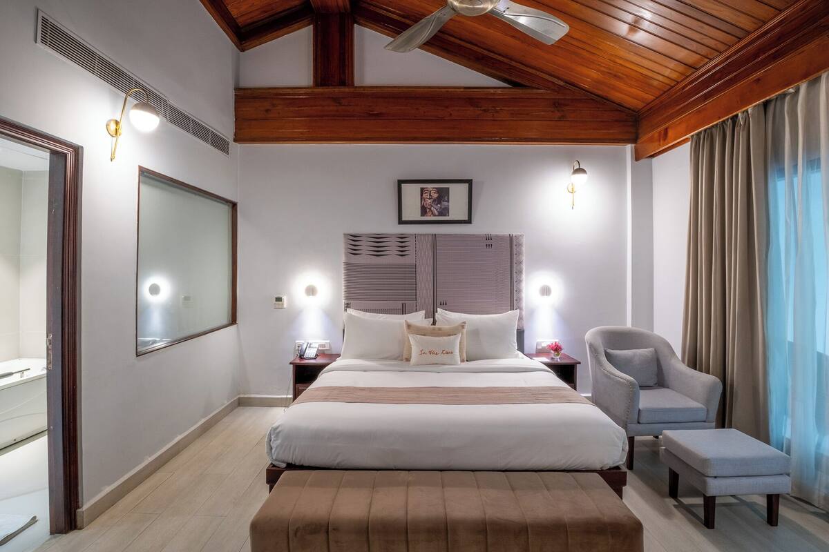 Quarto com cama grande, mesas de cabeceira, uma cadeira e ventoinha no teto.