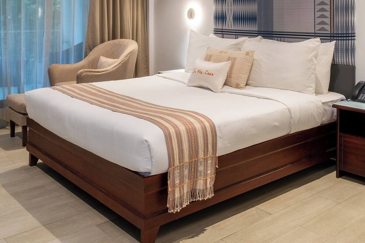 Um quarto de hotel moderno com uma cama grande, uma cadeira, uma mesinha de cabeceira e uma luminária fixada na parede.