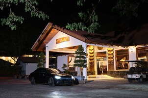 Uma área de recepção com uma placa, um carro e um carrinho de golfe em frente a um edifício com telhado inclinado e colunas.