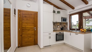 Cozinha com armários brancos, uma porta de madeira, micro-ondas e uma fruteira no balcão.