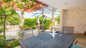 Um pátio externo com mesa e cadeiras, uma pérgola e um muro de pedra.