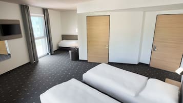 Quarto de hotel com duas camas, televisão, escrivaninha e janela com cortinas.