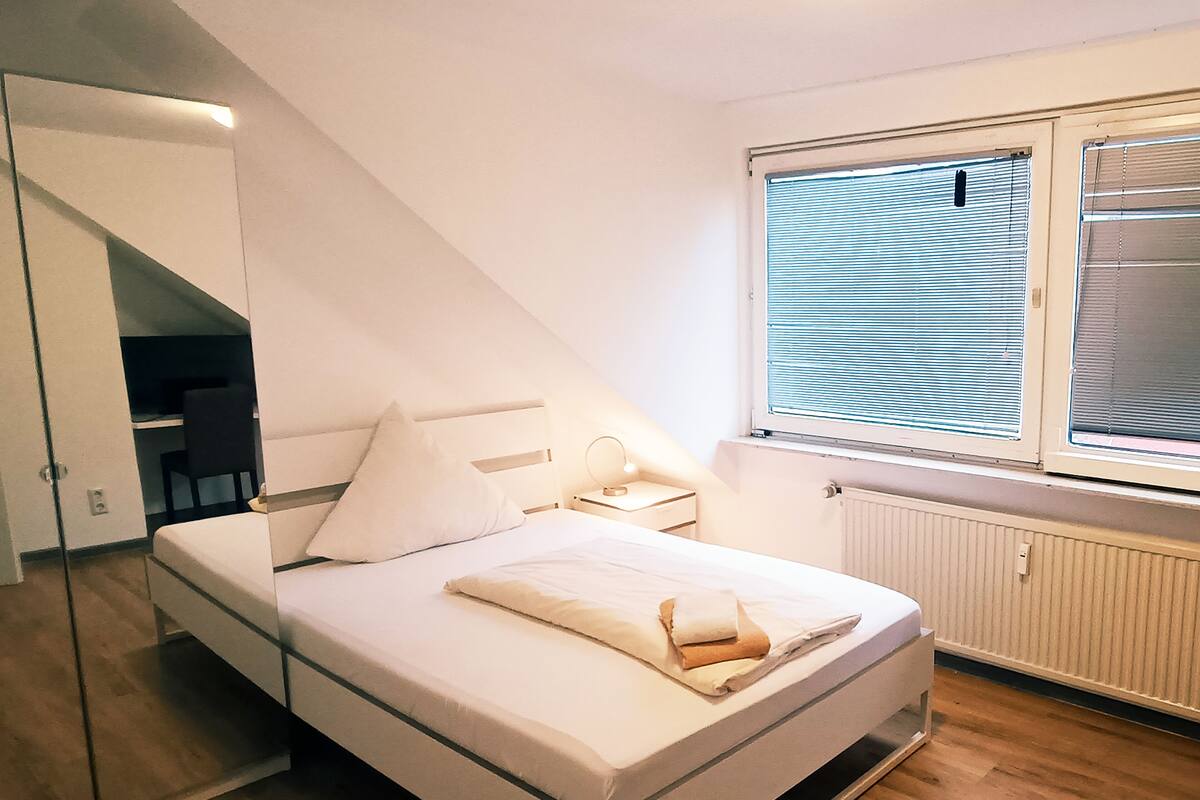 Quarto moderno com cama, mesa de cabeceira e janela com persianas.