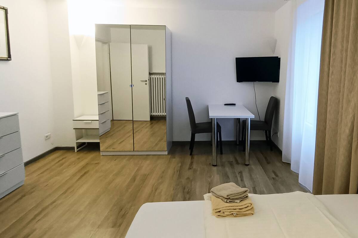 Quarto de hotel com cama, escrivaninha, cadeira, televisão e guarda-roupa.