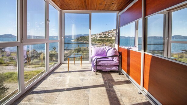Varanda com vista para um lago e colinas, um sofá roxo e teto de madeira.