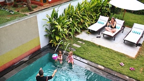 Piscina com cerca de proteção, espreguiçadeiras e área gramada com plantas.