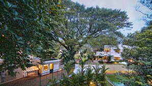 Um pátio com piscina, cercado por vegetação exuberante e um edifício branco com varanda.