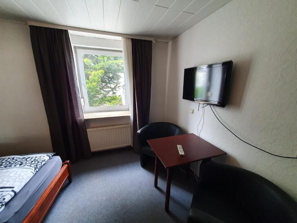 Quarto de hotel com cama, escrivaninha, cadeira, televisão e janela com cortinas.