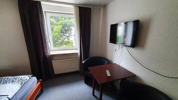 Quarto de hotel com cama, escrivaninha, cadeira, televisão e janela com cortinas.