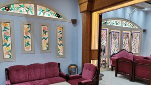 Quarto com sofá vermelho, mesa de centro de madeira e pequena mesinha lateral. Há quatro quadros florais na parede.