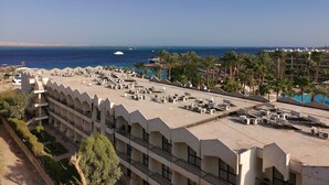 Um hotel com vários andares, unidades de ar condicionado externas, área de piscina e vista para o mar.