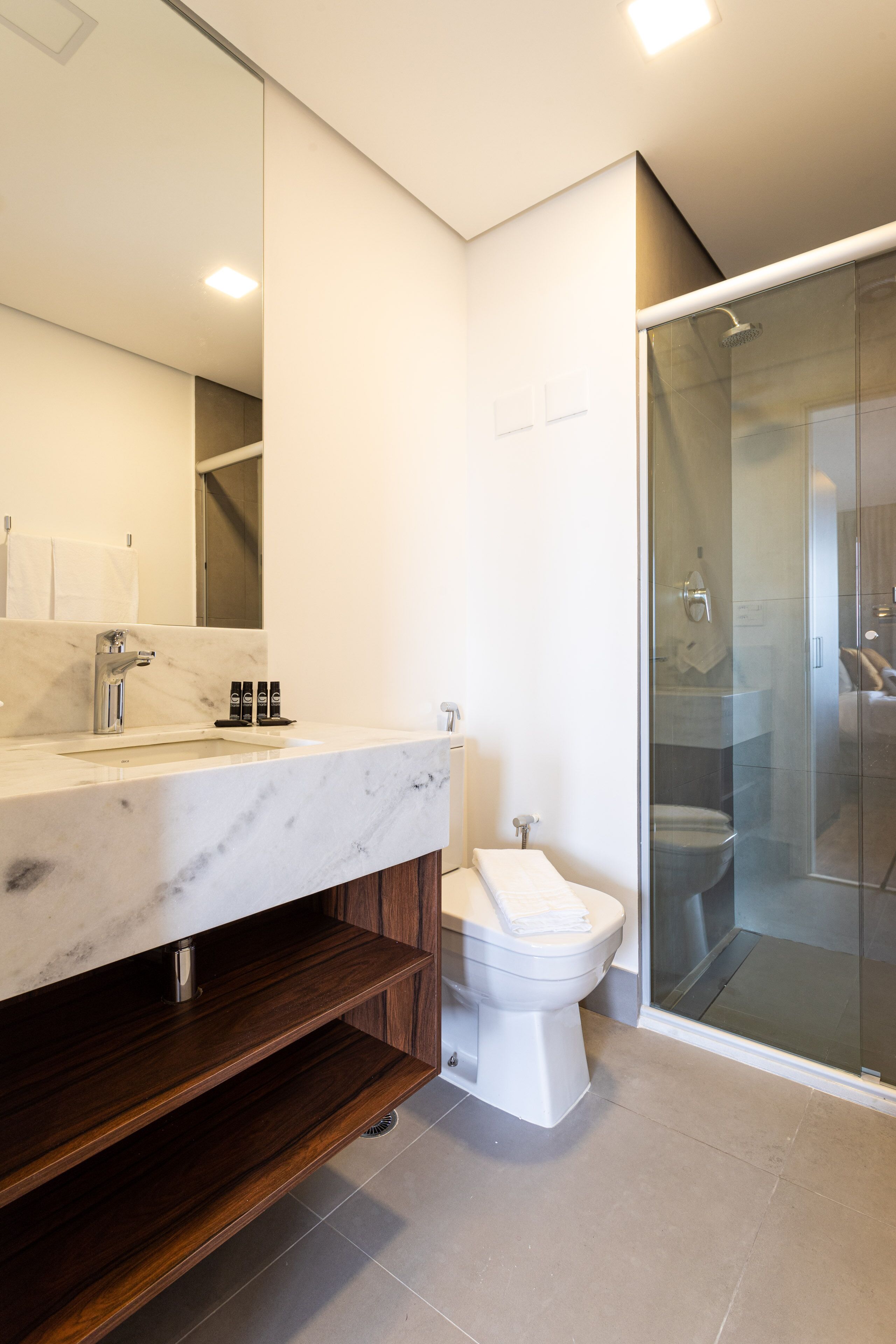 Um banheiro moderno com pia de mármore, vaso sanitário e chuveiro com box de vidro.