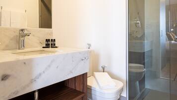 Um banheiro moderno com pia de mármore, vaso sanitário e chuveiro com box de vidro.
