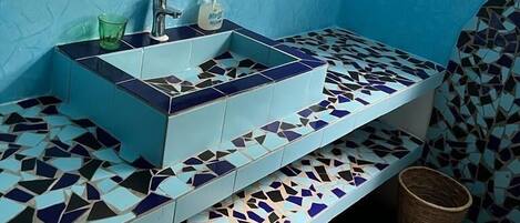 Um banheiro com piso azul ladrilhado, pia com espelho acima e cesta de vime no chão.