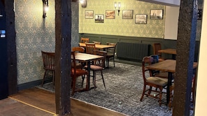 Interior de restaurante com papel de parede estampado, mesas e cadeiras de madeira e quadros nas paredes.
