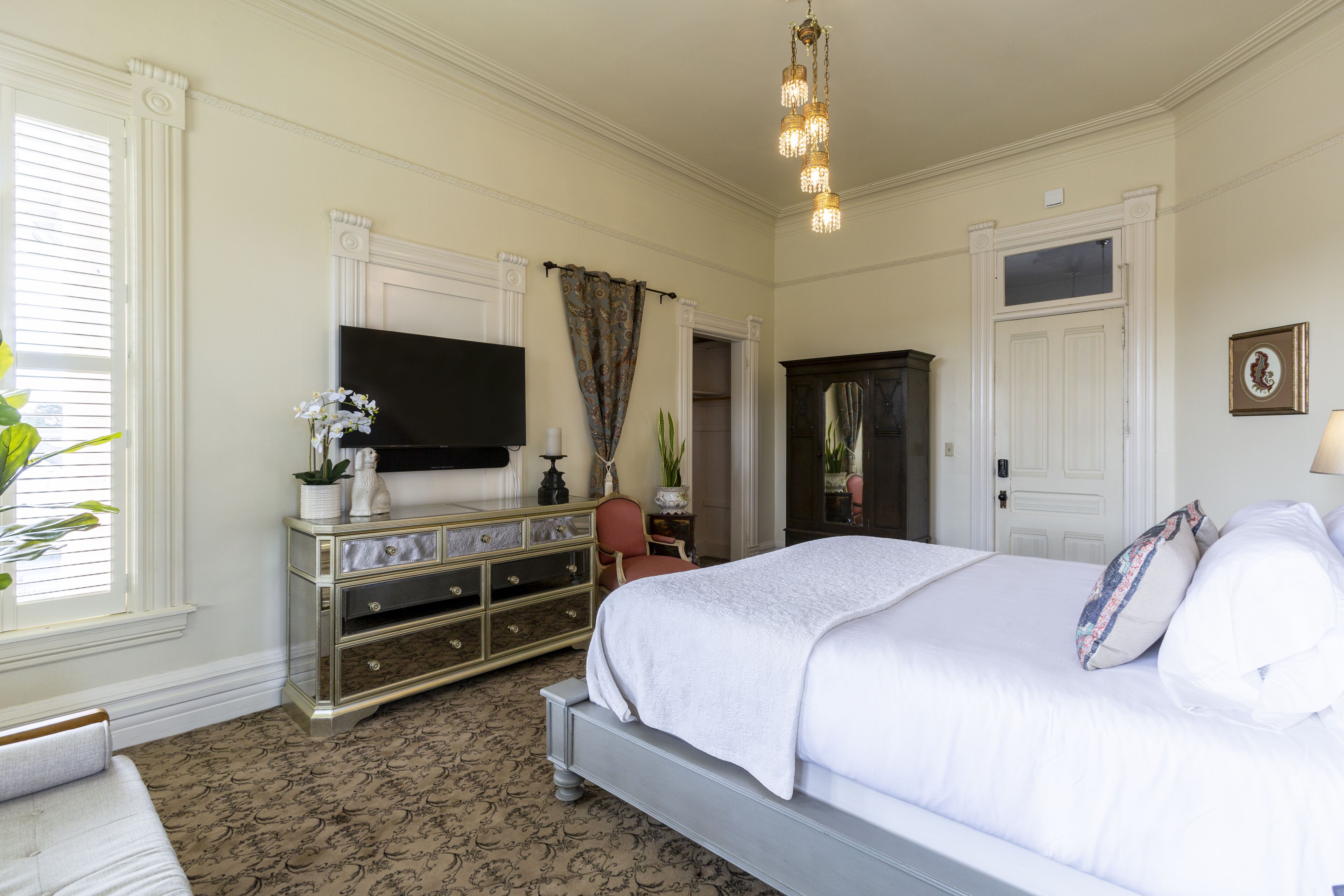 Quarto com cama, cômoda, televisão e lustre.