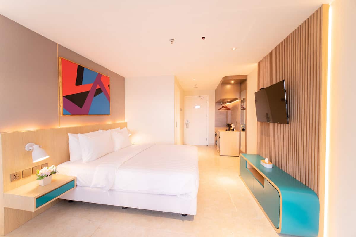 Quarto de hotel moderno com cama, mesa de cabeceira e televisão na parede.
