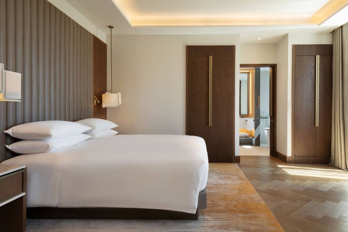 Quarto de hotel moderno com uma cama grande, uma mesinha de cabeceira, um guarda-roupa e um espelho.