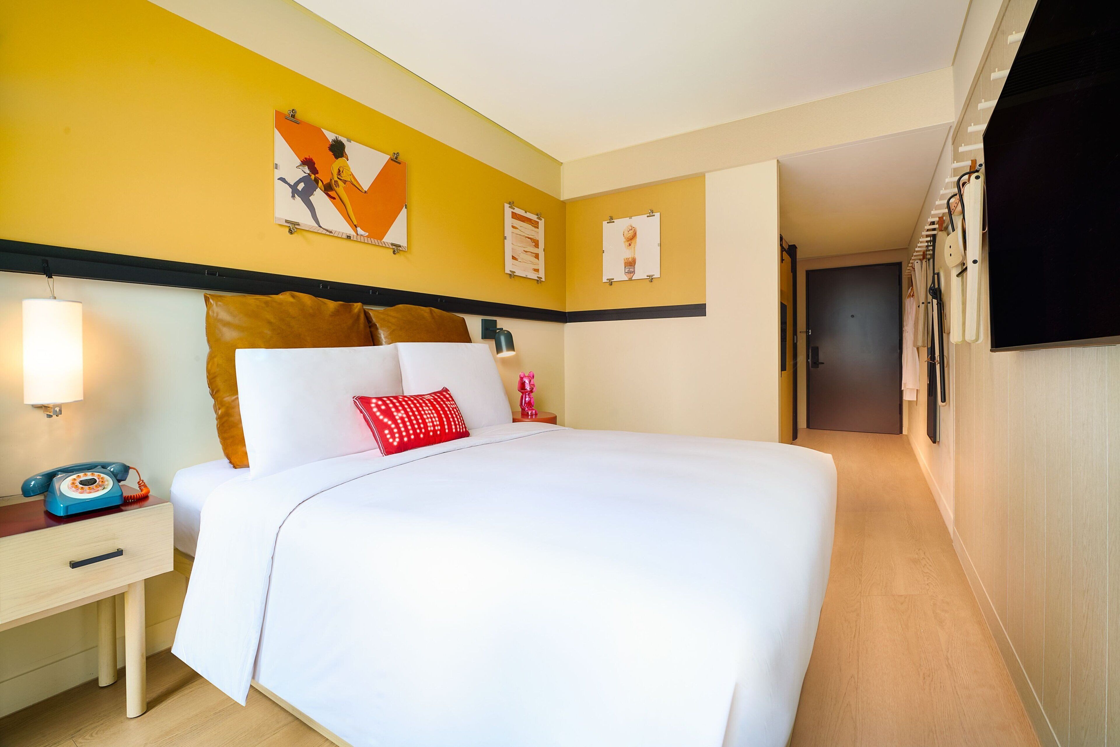 Quarto de hotel com uma cama grande, mesa de cabeceira com telefone e televisão na parede.