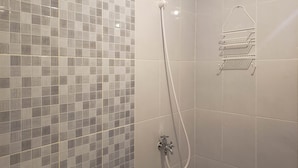 Uma casa de banho com parede de chuveiro em azulejo, chuveiro manual, porta-toalhas fixado na parede e sanita.